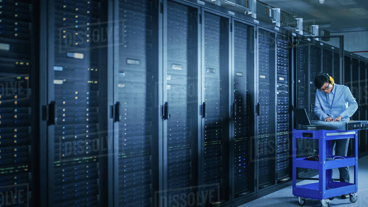 In the Modern Data Center: IT Technician Wearing Protective Headphones ...
