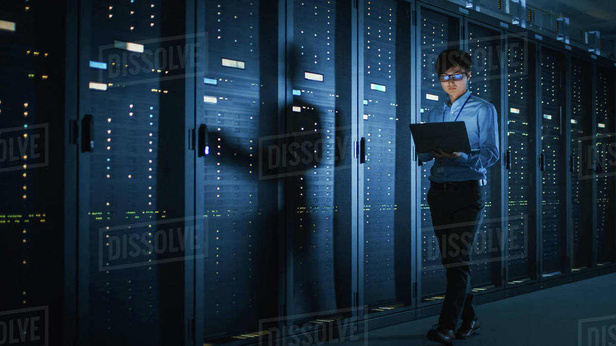 In Dark Data Center: Male IT Specialist Walks along the Row of Operational Server Racks, Uses ...