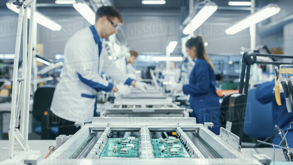 Shot of an Electronics Factory Workers Assembling Circuit Boards by Hand While it Stands on the ...