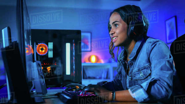 Pretty and excited black gamer girl in headphones is playing first ...