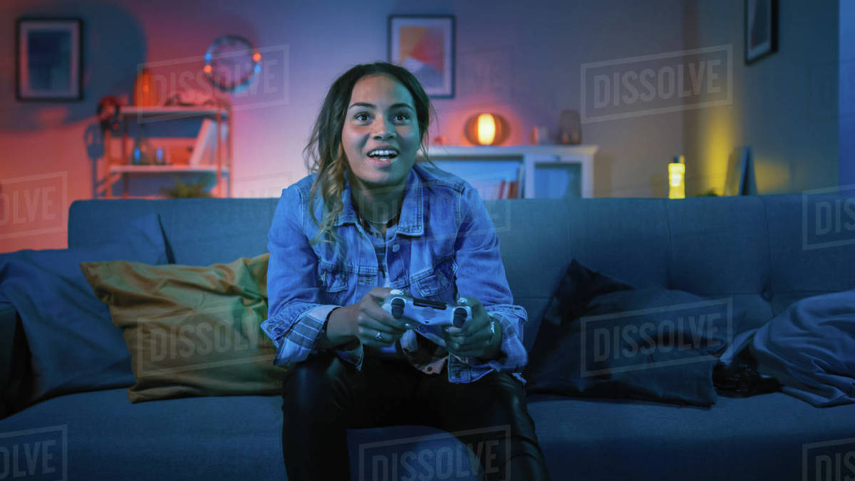 Beautiful excited young black gamer girl sitting on a couch and playing ...