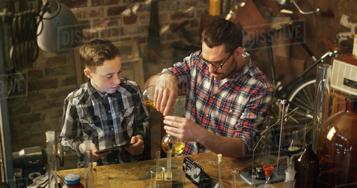 Father and son are making chemistry experiments while checking a tablet ...