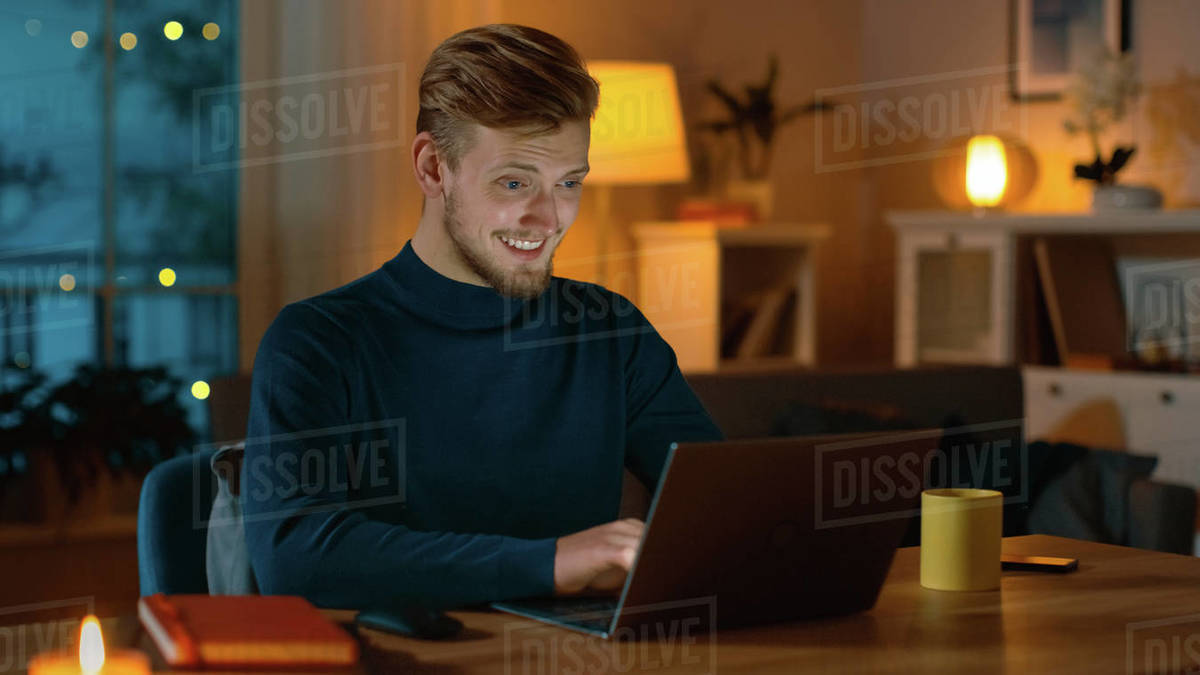 Handsome Smiling Man Works on a Laptop while Sitting at His Desk at ...