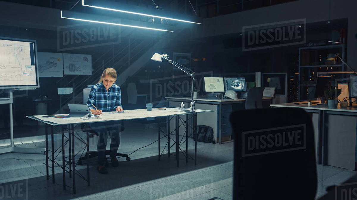 Female Engineer Sitting at Her Desk Works with Blueprints Laying on a ...