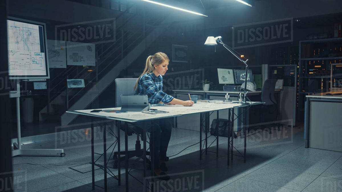 Female Engineer Sitting at Her Desk Works with Blueprints Laying on a ...