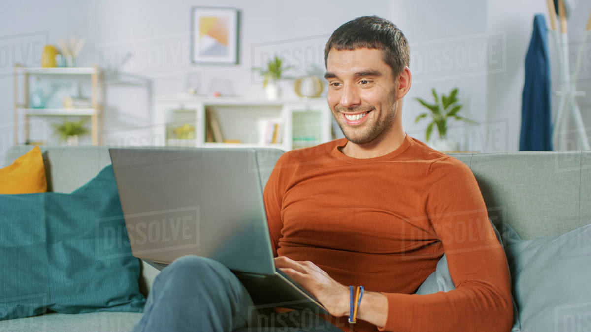 Handsome Man Uses Laptop Computer while Sitting on Sofa at Home. Man ...