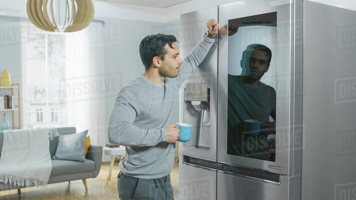Handsome Young Man is Standing Next to a Refrigerator While Drinking ...