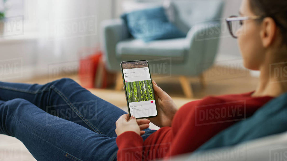 Young Woman at Home Lying on a Couch using Smartphone Scrolling Through ...