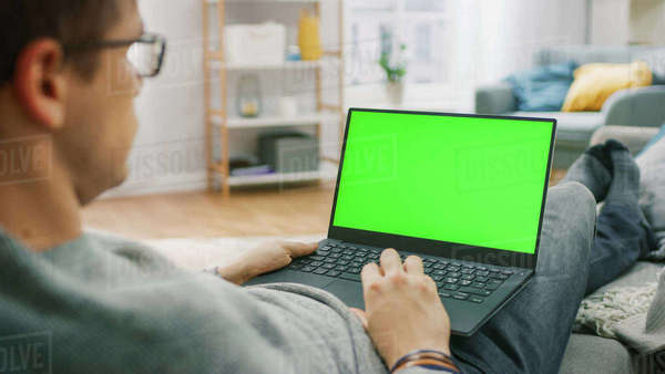 Man at Home Sitting on a Couch Working on Green Mock-up Screen Laptop ...