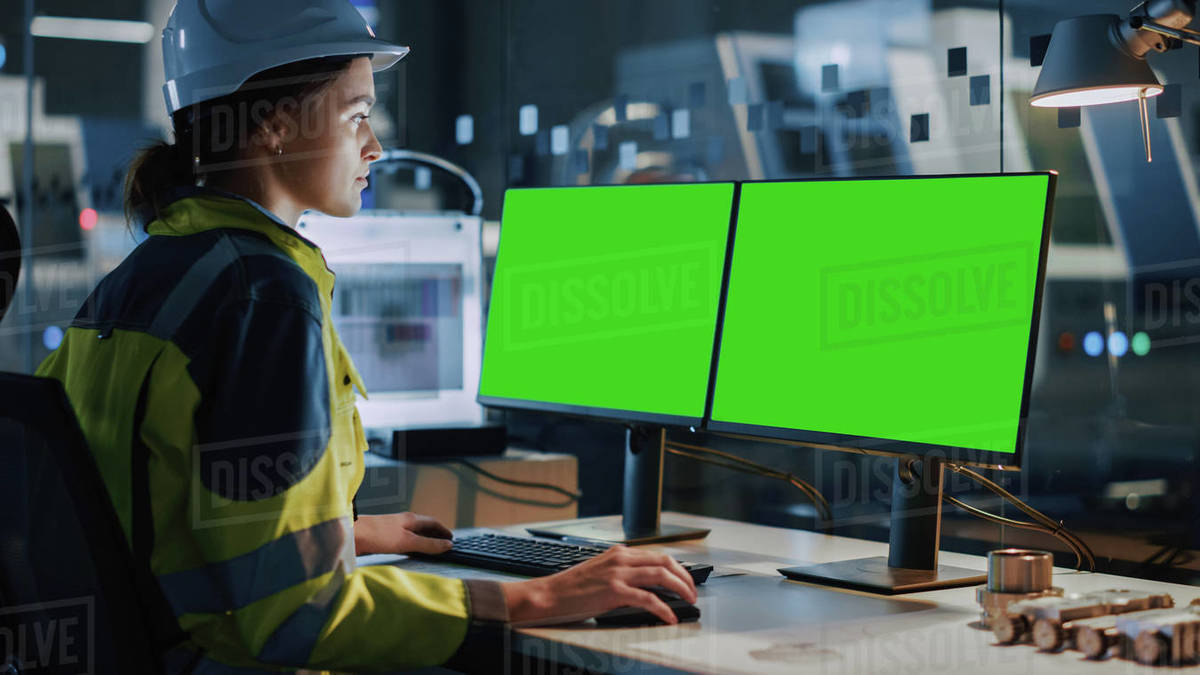 Young and Confident Industrial Female Engineer in Safety Vest and Hardhat is Working on Computer ...
