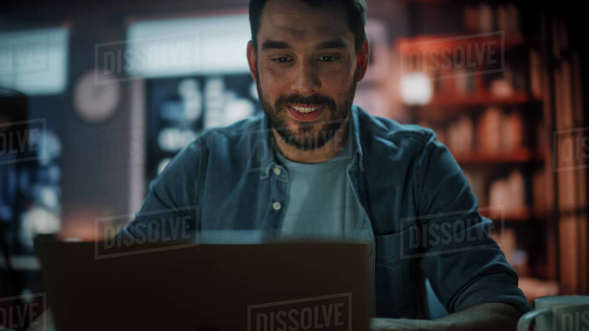 Man Working on Laptop Computer while Sitting at a Desk in Dark Cozy ...