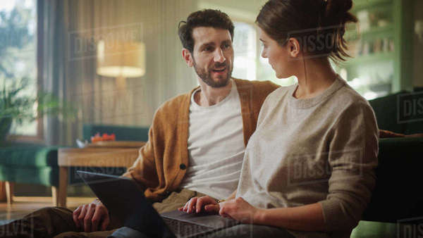 Couple Using Laptop Computer, while Sitting on the Living Floor room of ...