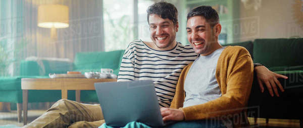 Gay Couple Using Laptop Computer, while Sitting on a Living Room Floor ...