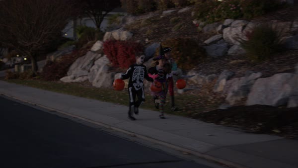 Tracking shot of children running in neighborhood at night on Halloween ...