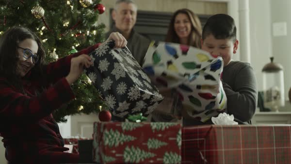 Parents watching son and daughter ripping open wrapping paper on ...