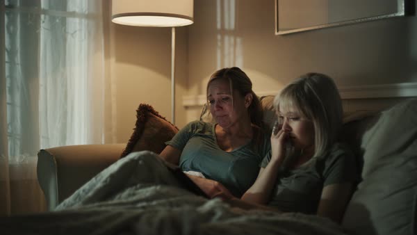 Crying mother and daughter on sofa streaming sad movie on digital ...