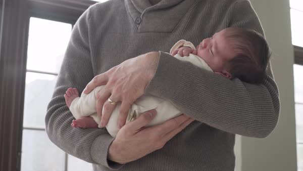 Close-up shot of a man carrying his sleeping newborn baby boy at home ...