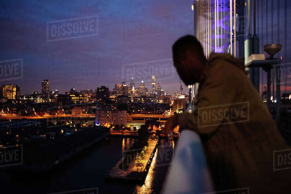 Man looking at illuminated cityscape while standing on bridge at night ...