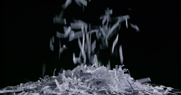 Shredded paper pieces falling against black background forming a mound ...