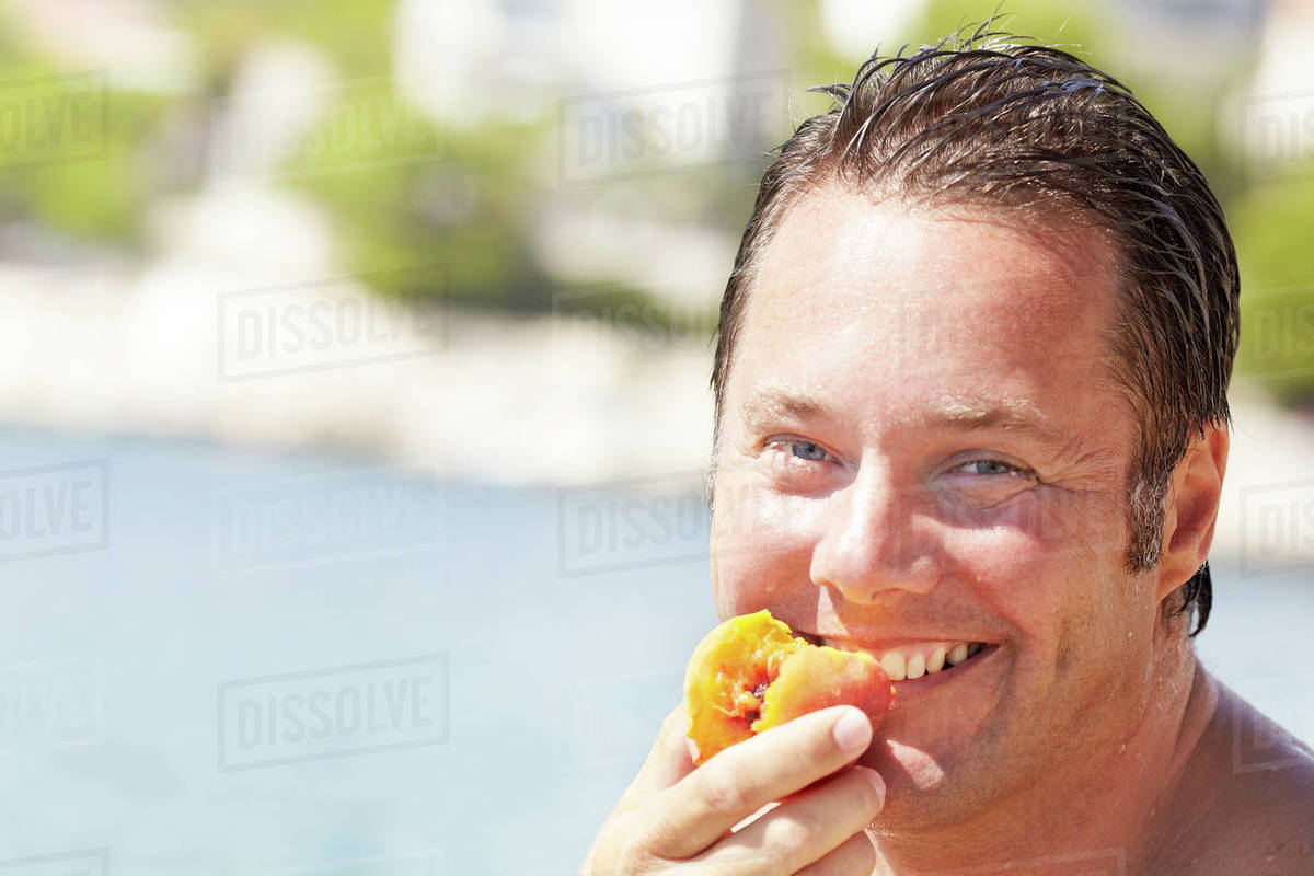 Smiling man eating peach - Royalty-free Stock Photo | Dissolve
