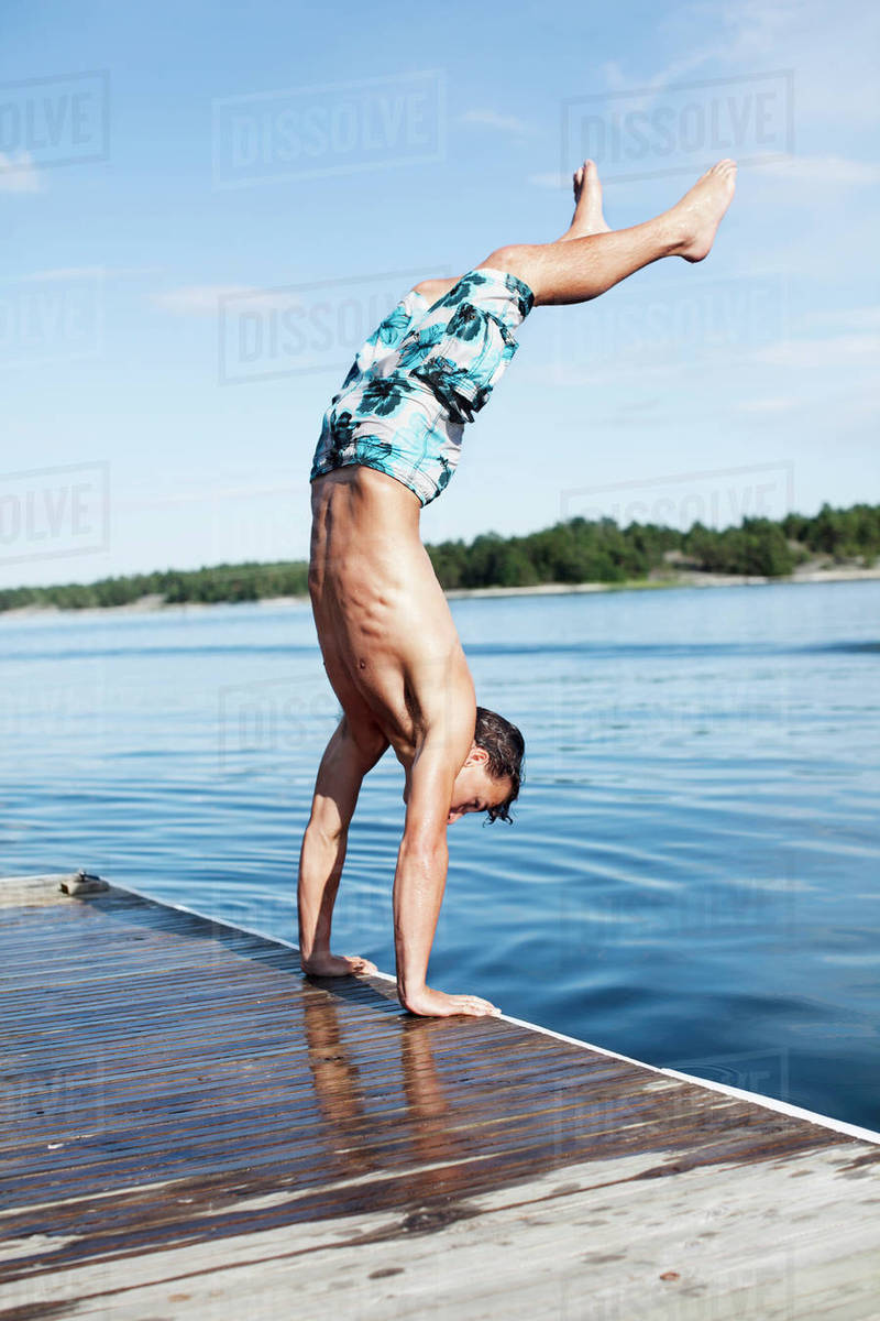 Teenage boy doing handstand on jetty - Royalty-free Stock Photo | Dissolve