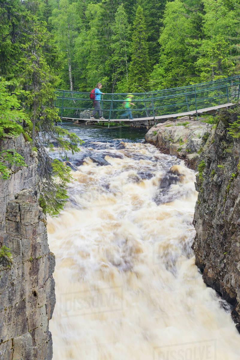 Person crossing footbridge over river - Royalty-free Stock Photo | Dissolve