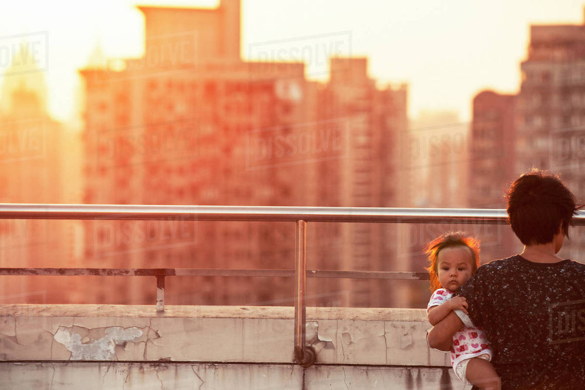 Woman with baby on roof, cityscape at sunset on background - Stock ...