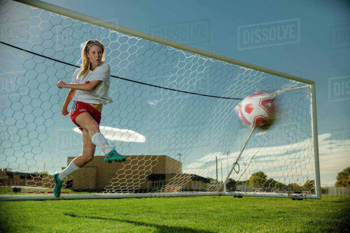 Low angle view of goalie jumping and kicking soccer ball in goal under ...