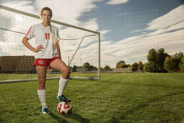 Low angle view of athlete standing with soccer ball on field under blue ...
