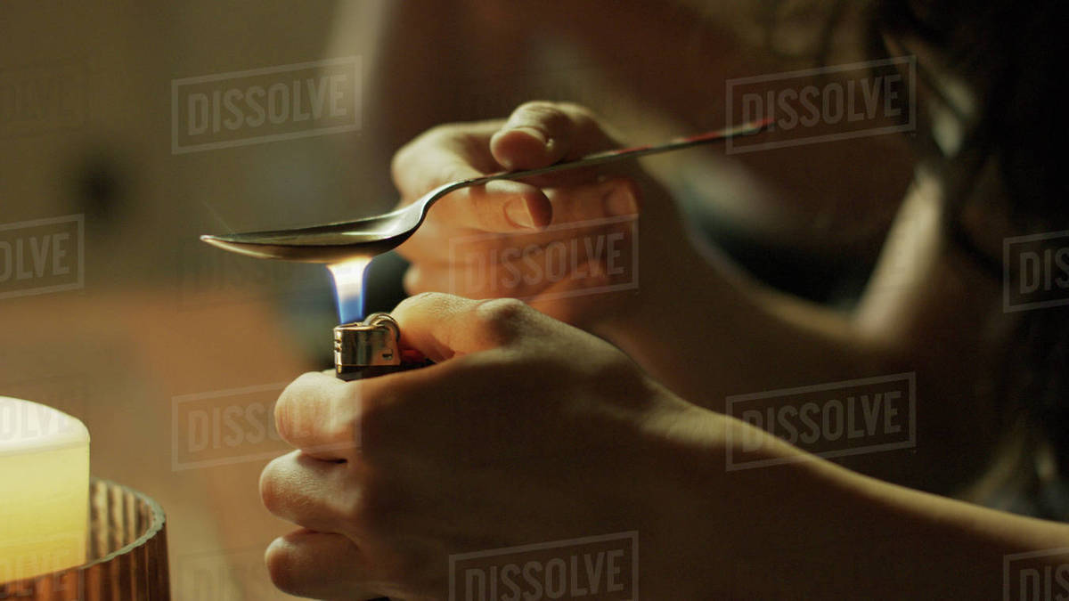 Close up of drug addict cooking drugs in spoon with lighter on dingy ...