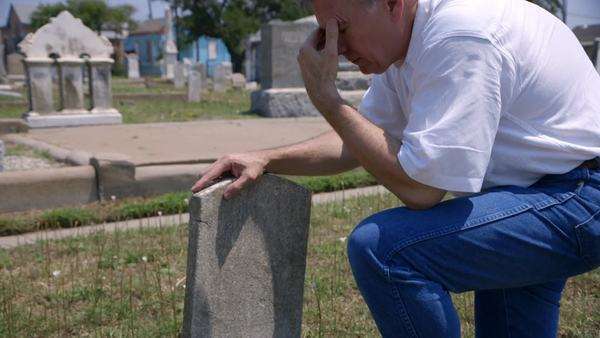 A grieving man kneeling at by an old worn and faded gravestone. - Stock ...