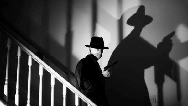 Deep shadows surround a man with a gun slowly walking down a staircase ...