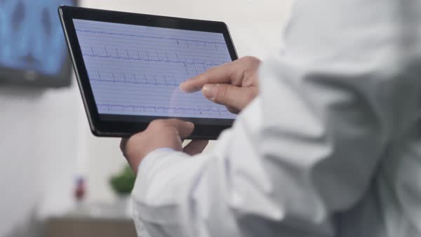 Doctor cardiologist from behind looks ecg electrocardiogram record on ...