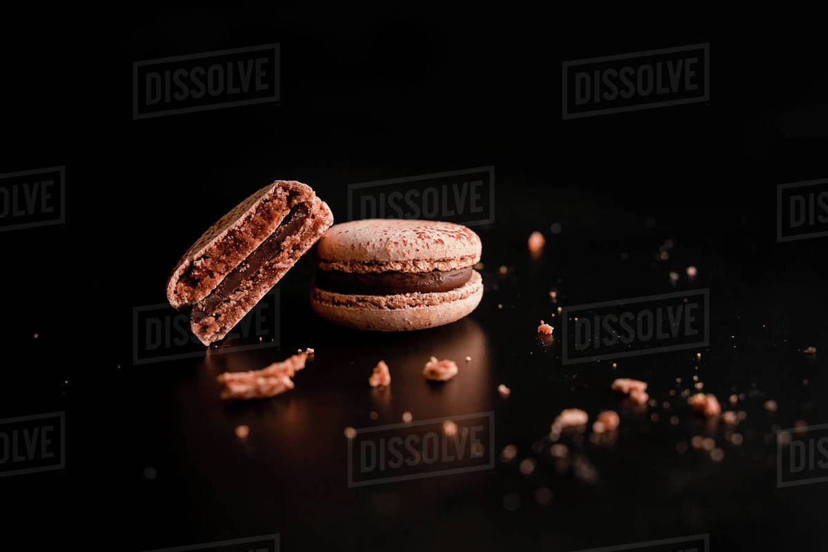 several chocolate macaroons cut in half on a dark background close up ...