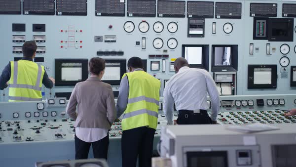 Workers in power plant control room looking at control panel and ...