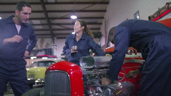 Team of male and female mechanics working on a car engine in garage ...