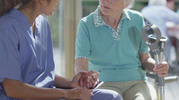 Caring nurse giving support to elderly female patient in a hospital or ...