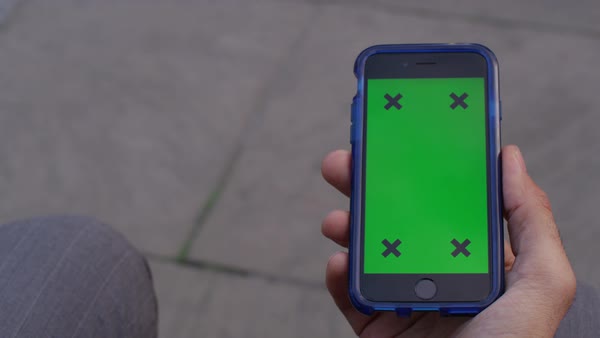 Close-up of hand using a smartphone with green screen display outdoors ...
