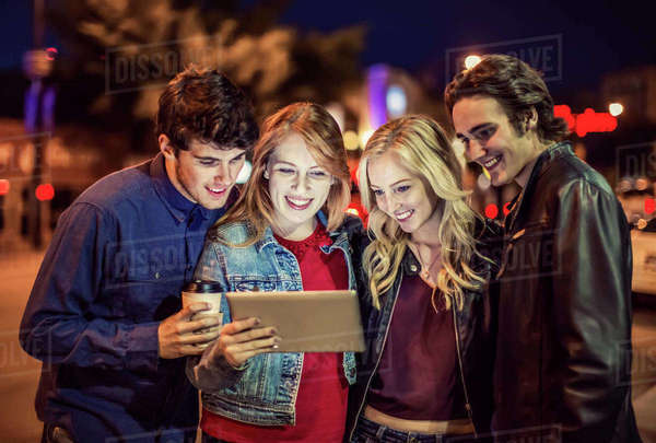 A group of four friends huddle together on a sidewalk looking at a ...