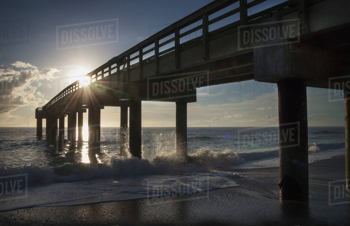 Sunlight at sunrise streaming through the rails of an ocean pier as ...