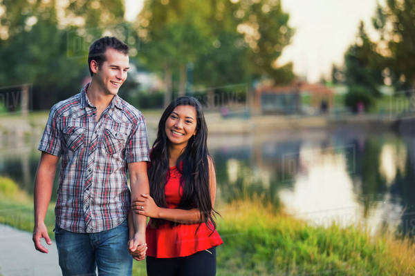 Mixed race couple spending quality time together walking around a lake ...