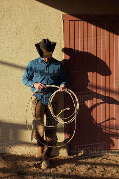 Agriculture - Cowboy with a lasso rope standing against a barn in ...