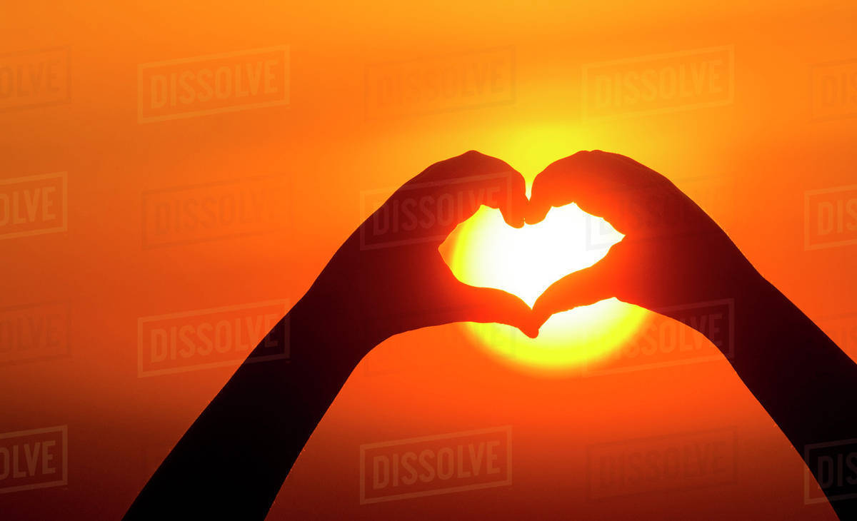Hands making a heart shape in front of the sun; United Kingdom ...