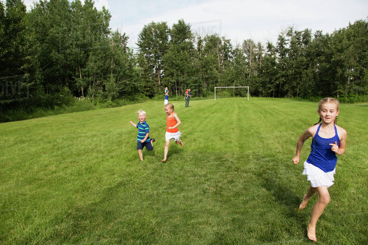 Kids running across a grass field in a park with the parents in the ...