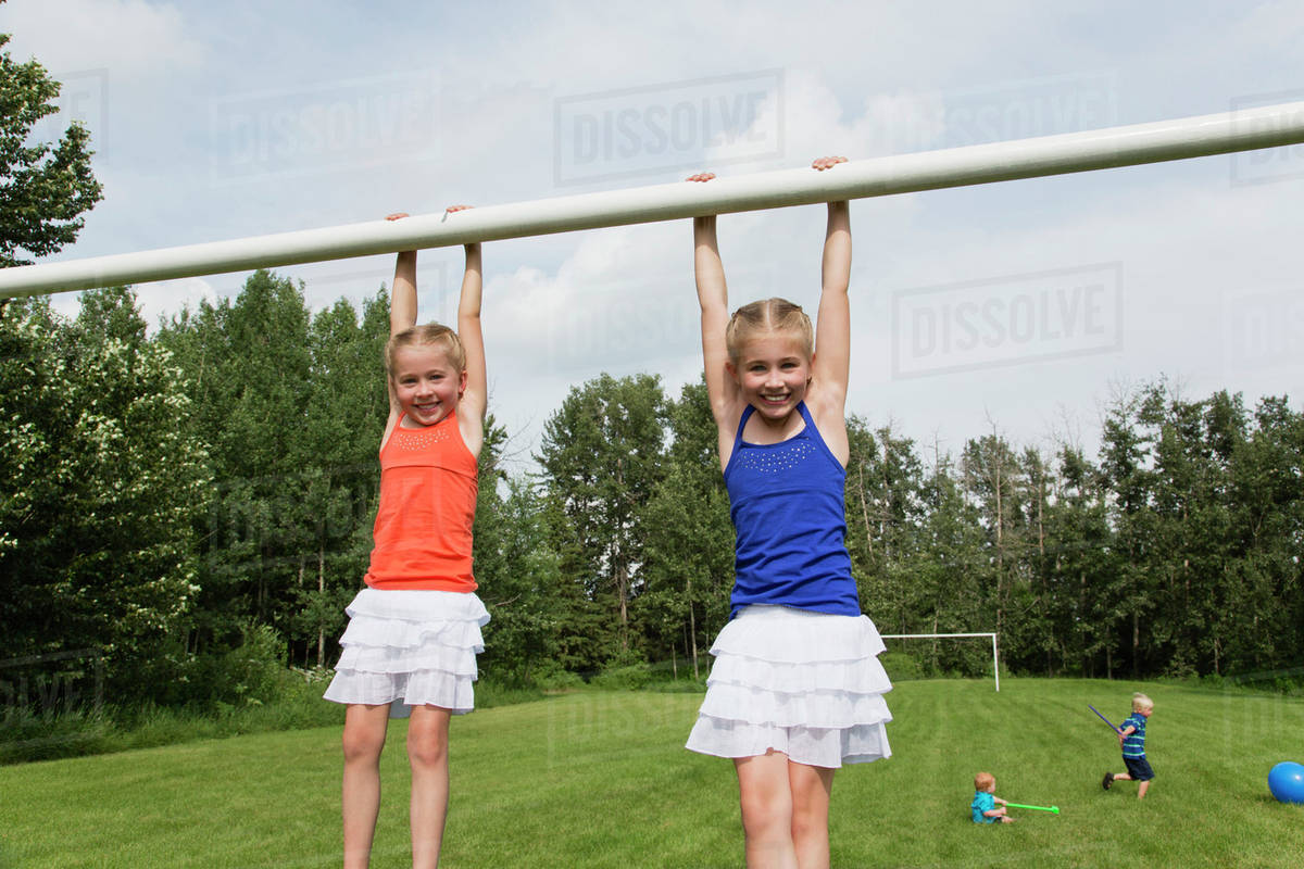 Two girls holding onto the crossbar of a soccer goal post in a park ...