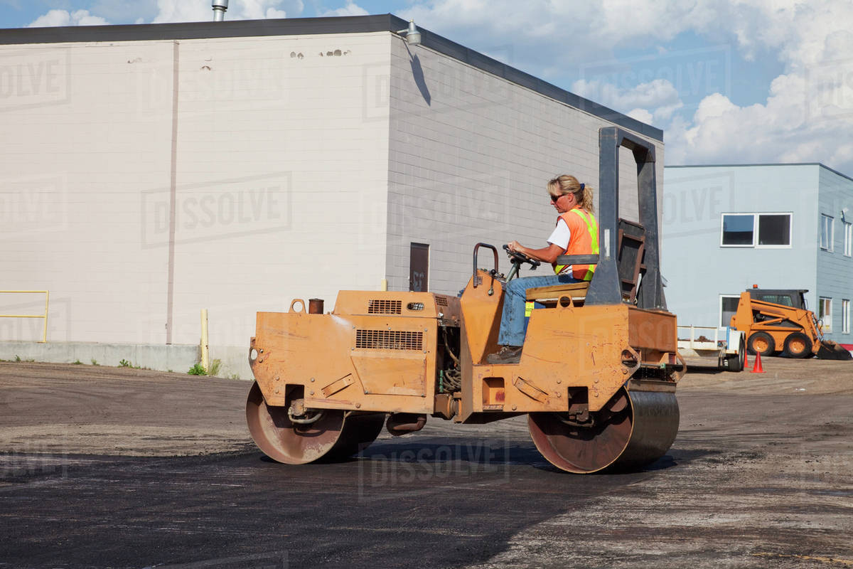 Female operator driving steam roller repairing pot holes in a parking ...