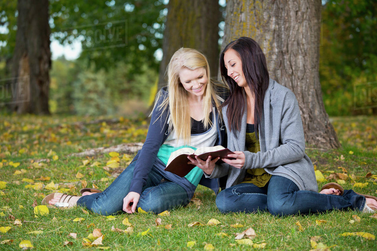 Two teenage girls reading the Bible together in a park; Edmonton ...