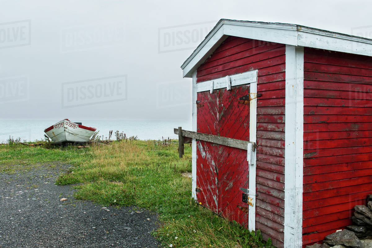 A red weathered shed and a boat on the shore at the coast; Sally's Cove ...