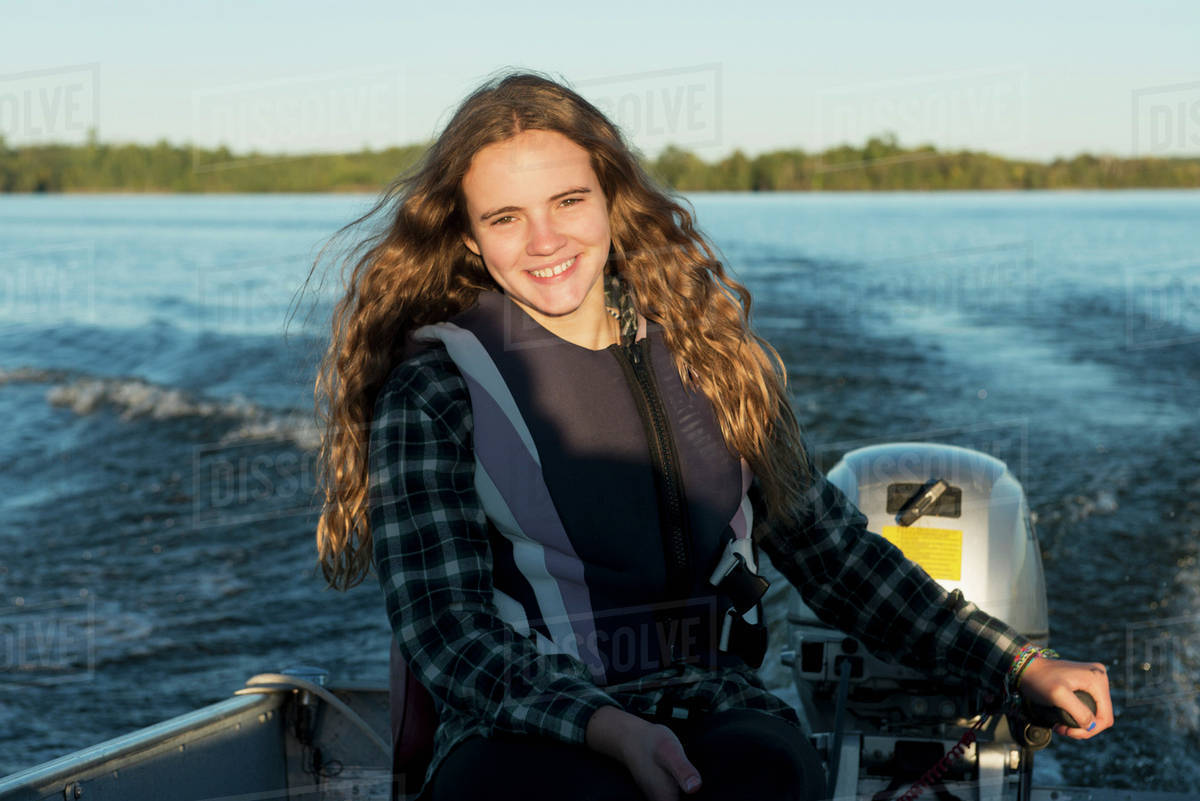 A teenage girl sits by the motor at the back of a motorboat with her ...
