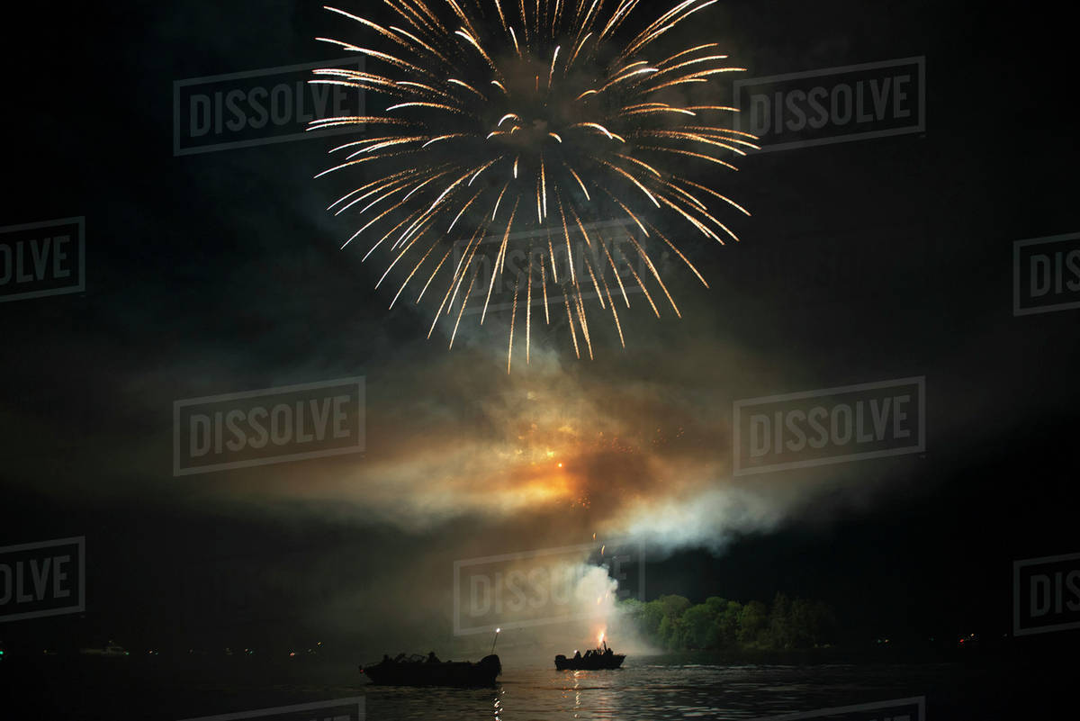 Fireworks display over a lake illuminating the boats on the water ...